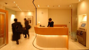 Uma área de recepção de hotel com um balcão curvo, um relógio na parede e um quiosque de autoatendimento.