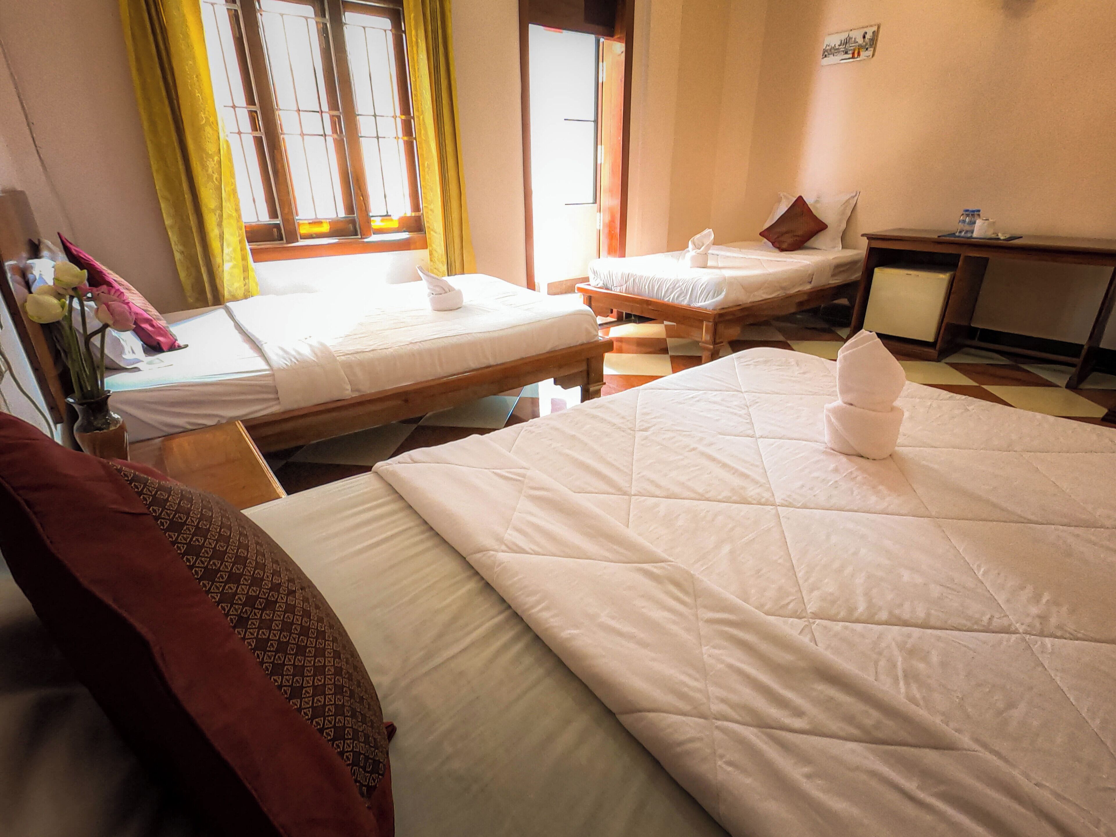 Quarto de hotel com duas camas, uma mesinha e janela com cortinas amarelas.