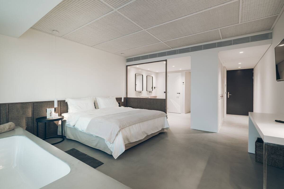 Quarto de hotel moderno com uma cama grande, banheiro privativo, escrivaninha e closet espaçoso.