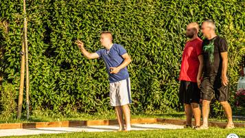 Três pessoas em um jardim, com uma sebe ao fundo.
