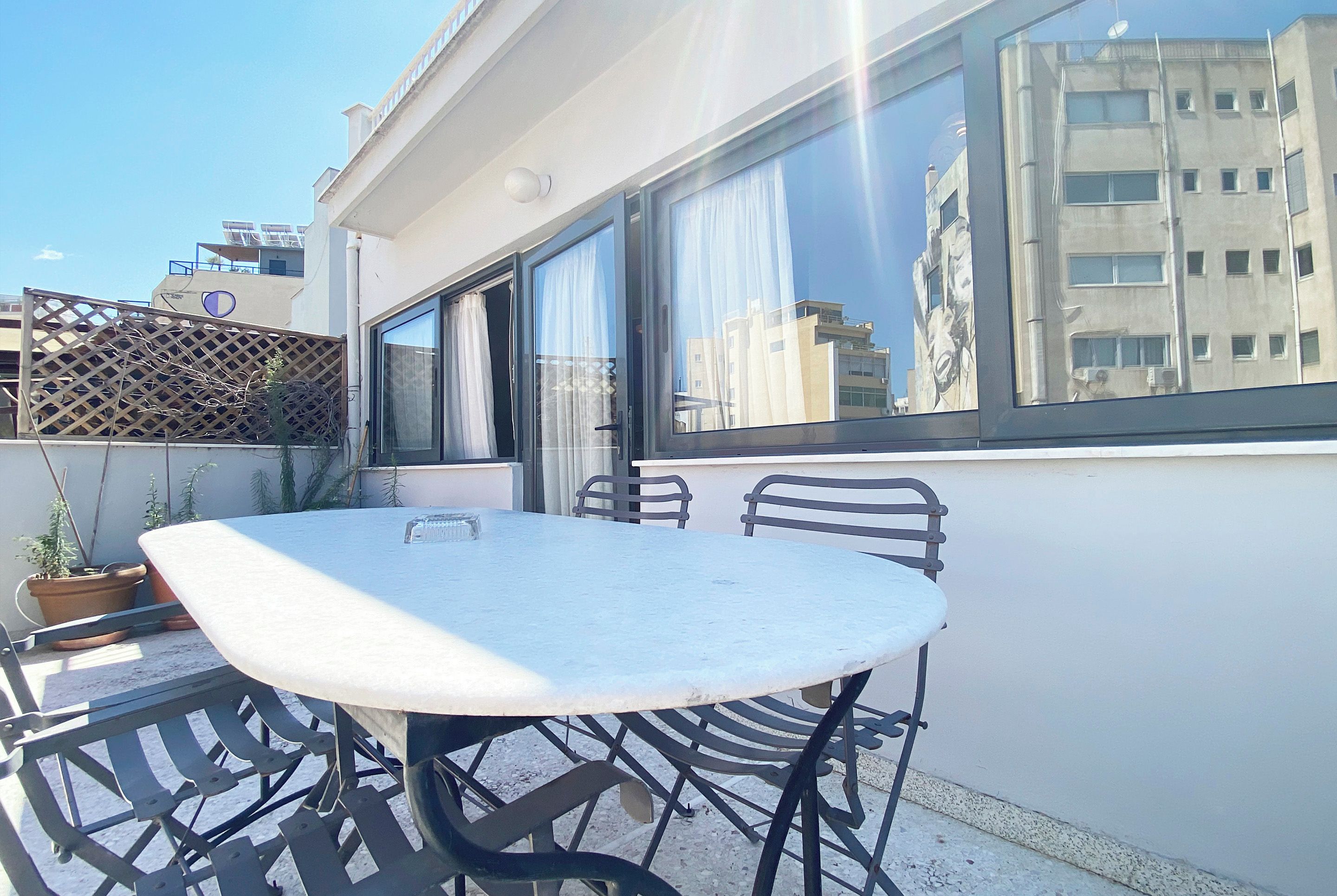 Varanda com mesa e cadeiras, um vaso de planta e vista para um prédio.