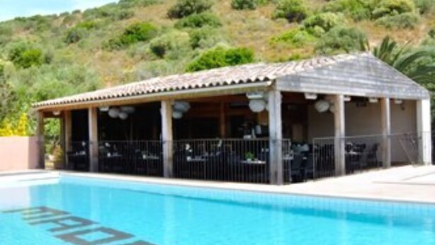 Piscina com área de estar coberta e uma colina ao fundo.