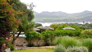 Um jardim com muros de pedra, piscina e guarda-sóis.