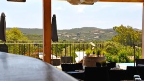 Uma área de refeições ao ar livre coberta, com vista para colinas e vegetação.