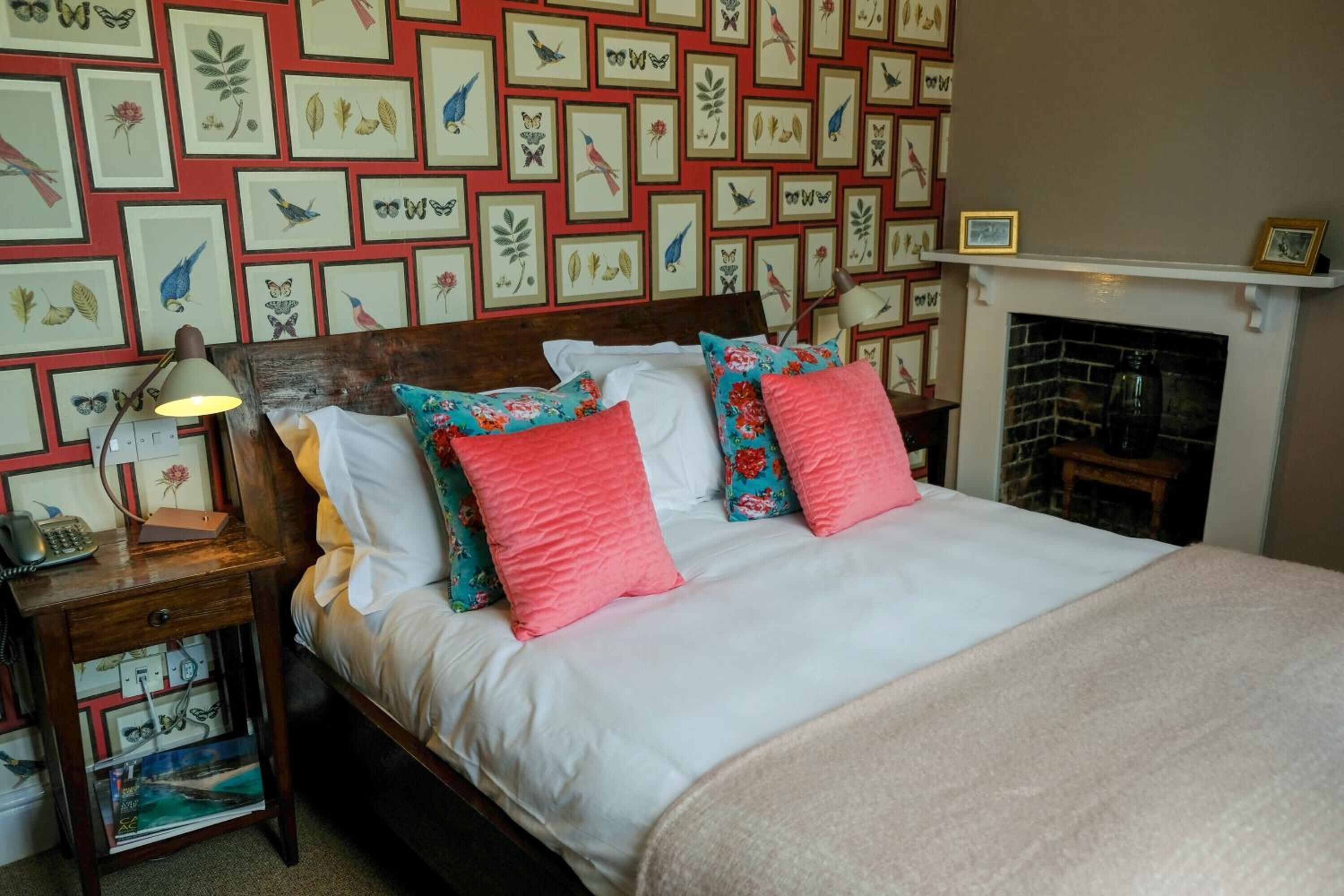 Cama bem arrumada com almofadas florais, abajur e quadro com passarinhos na parede.