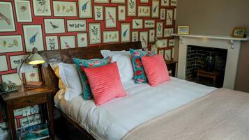 Cama bem arrumada com almofadas florais, abajur e quadro com passarinhos na parede.