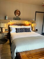 Cama bem arrumada com cabeceira de madeira, duas luminárias de apoio e um objeto decorativo na parede acima da cama.