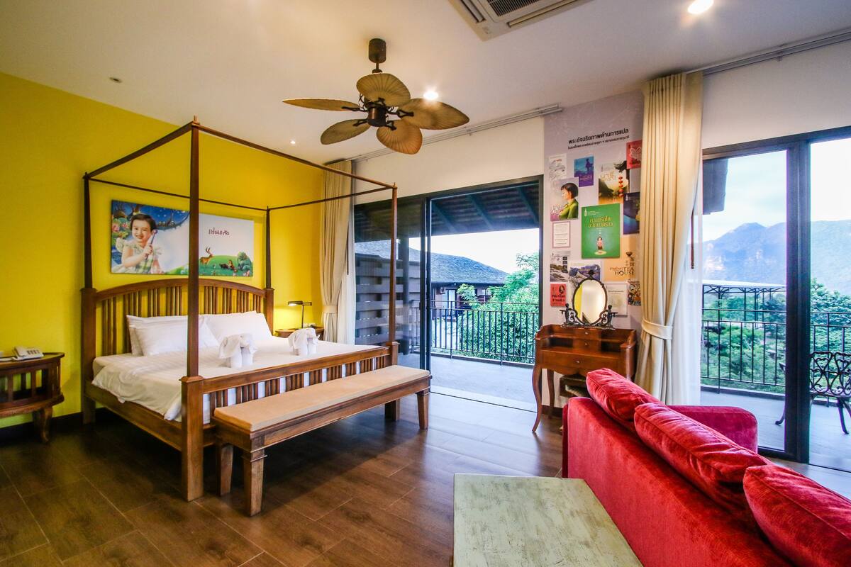 Um quarto com uma cama de dossel, um sofá vermelho, um banco de madeira e um ventilador de teto.