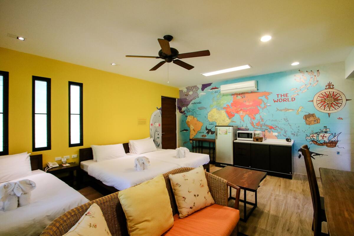 Quarto de hotel com duas camas, uma mesa de jantar, área de cozinha e um mapa-múndi na parede.