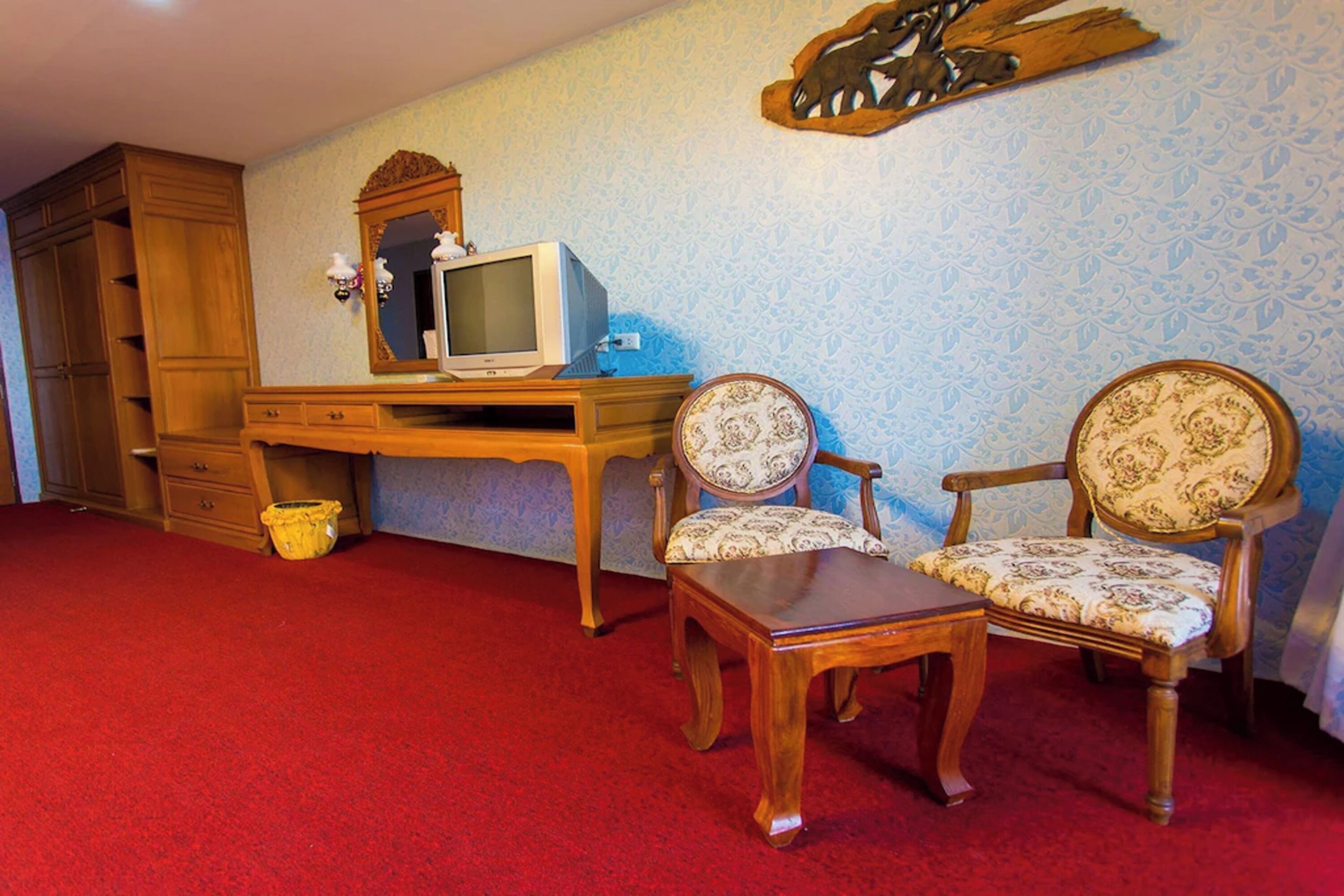 Um quarto com uma escrivaninha de madeira, duas cadeiras, uma televisão e um espelho.