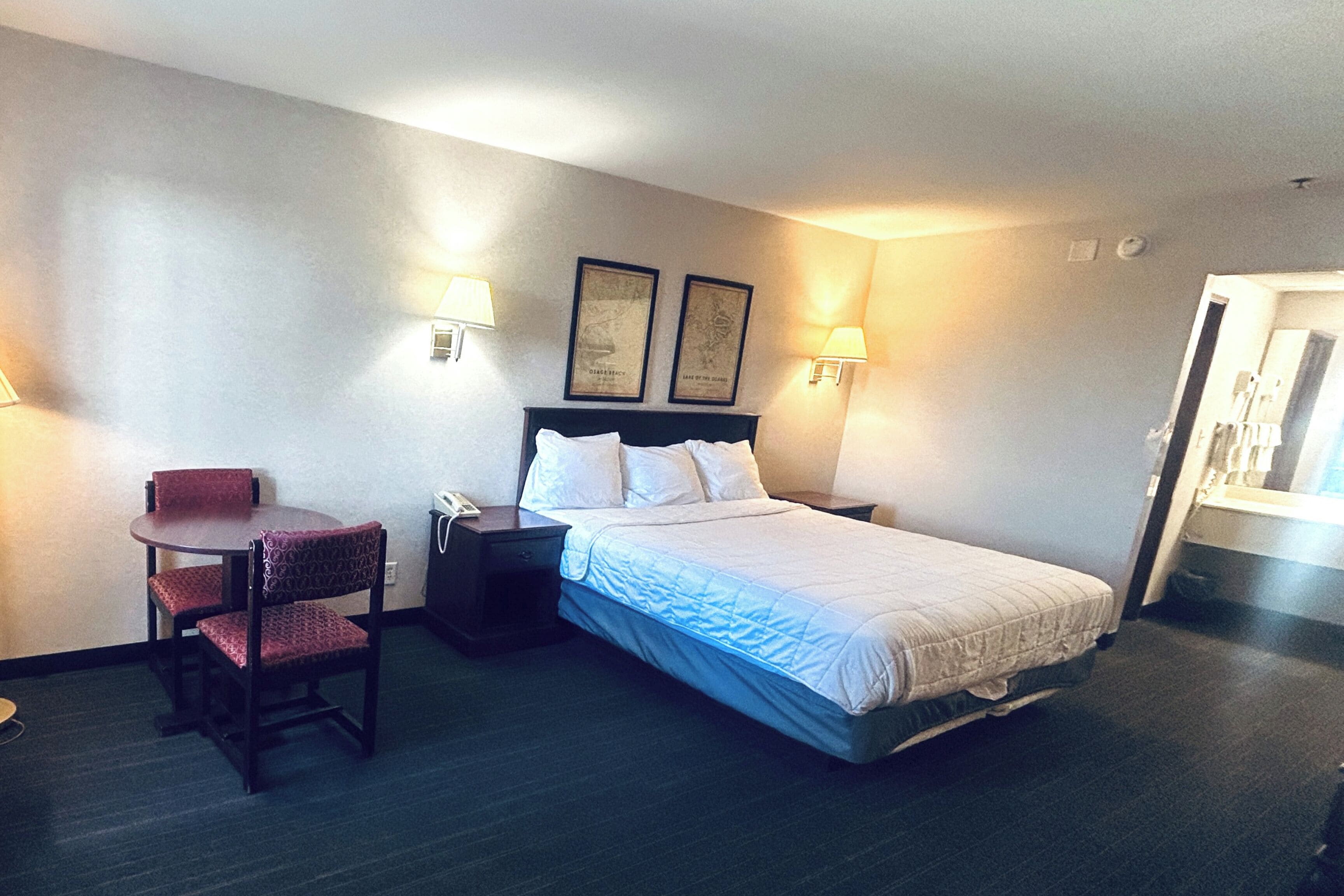 Quarto de hotel com cama, escrivaninha, cadeira e duas luminárias fixadas na parede.