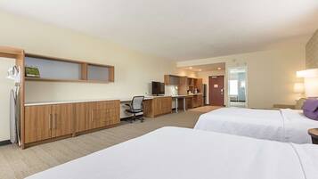 Quarto de hotel com duas camas, uma escrivaninha com computador, uma cadeira e uma kitchenette.