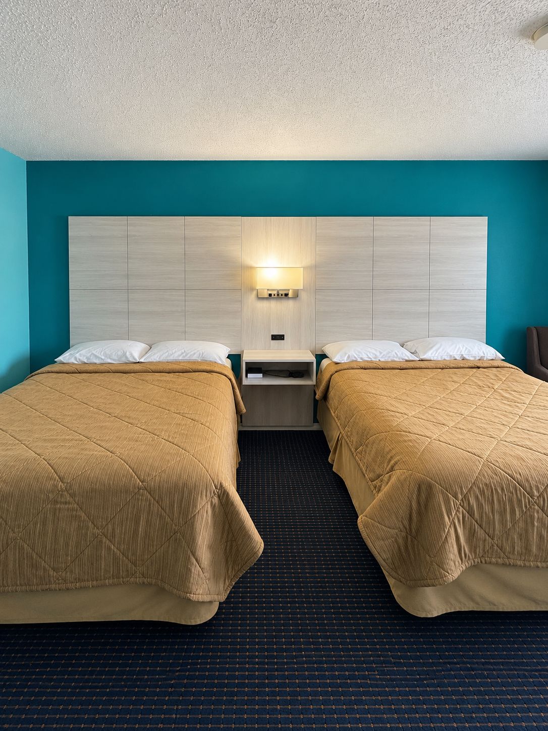 Quarto de hotel com duas camas, uma mesa de cabeceira e uma luminária fixada na parede.