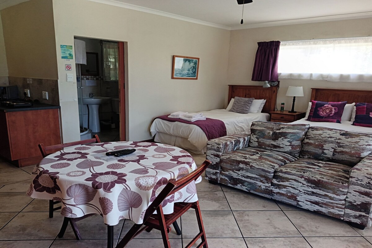 Quarto de hotel com cama, sofá, mesa de jantar e cozinha compacta.