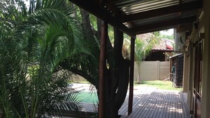 Um deck de madeira com área coberta, cercado por vegetação exuberante e uma piscina.