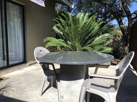 Mesa redonda com duas cadeiras, uma planta samambaia grande e uma porta de vidro.