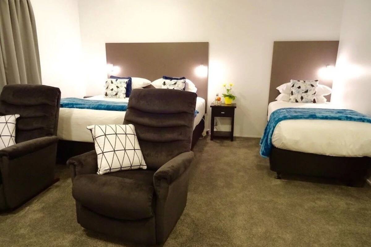 Quarto de hotel com duas camas, um sofá e uma mesa de cabeceira com abajur.