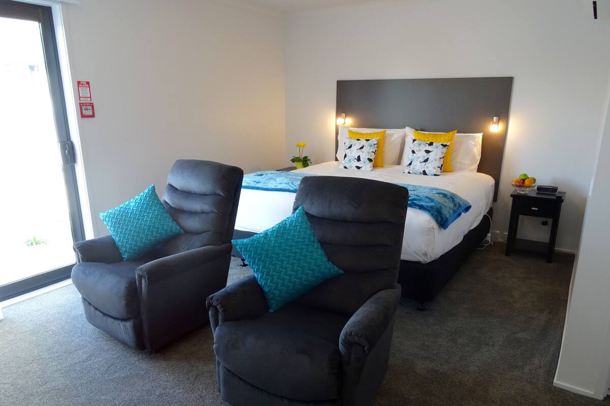 Quarto de hotel com uma cama, duas poltronas, uma mesinha de cabeceira e uma pequena mesa com uma fruteira.