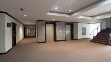 Corredor de hotel com piso carpeteado, escada e várias portas de acesso aos quartos.