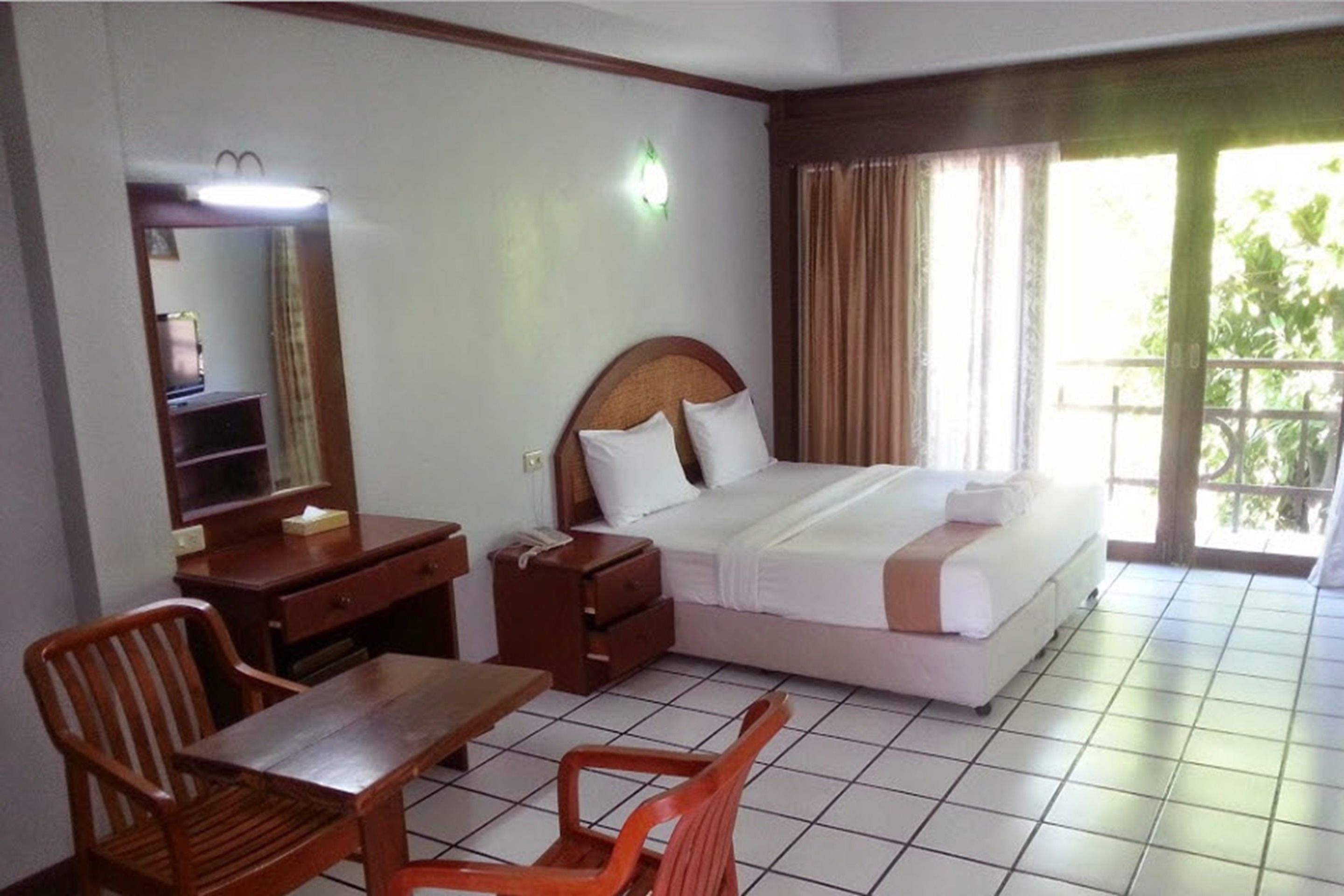 Quarto de hotel com cama, escrivaninha, cadeira, mesa de cabeceira, espelho e janela com cortinas.
