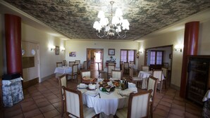 Uma sala de jantar com várias mesas postas para refeições, um candelabro e piso de azulejos.