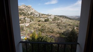 Uma varanda com vista para uma paisagem montanhosa, um edifício com telhado vermelho e céu claro.