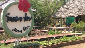 Um letreiro com o texto 'Tamarindo tree down for' rodeado por um jardim com diversas plantas e um edifício rústico ao fundo.