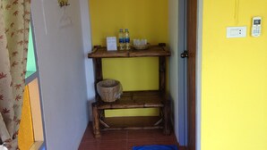 Quarto com prateleira de madeira com garrafas e uma cesta, porta com interruptor de luz e termostato fixado na parede.