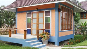 Uma casa pequena, térrea, com telhado de telhas, varanda frontal com degraus e um pequeno jardim com flores.