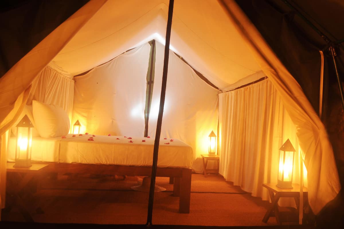 Alojamento em tenda com cama, almofadas, um banco e duas lanternas.