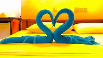 Cama com colcha e almofadas amarelo-claras, e duas toalhas azuis dispostas em formato de coração.