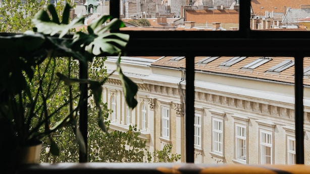 Vista da janela com uma paisagem urbana, prédios e uma estátua numa colina.