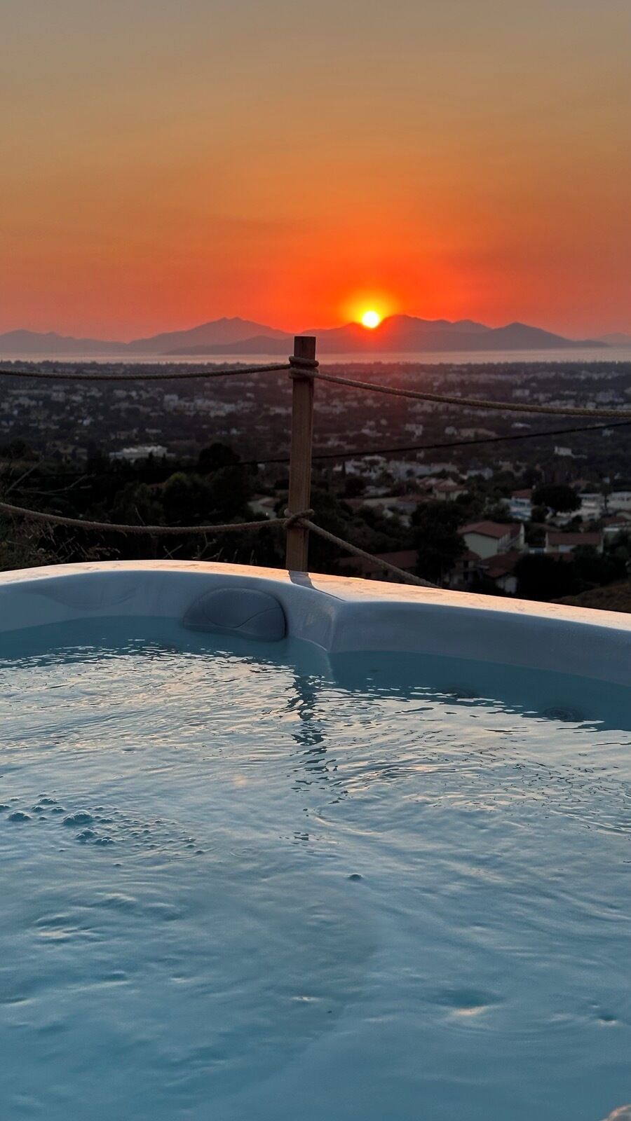 Uma banheira de hidromassagem com vista para um pôr do sol sobre a paisagem urbana.