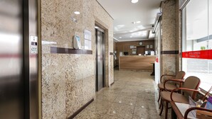 Um saguão de hotel com balcão de recepção, área de atendimento e um espaço de estar com cadeiras.