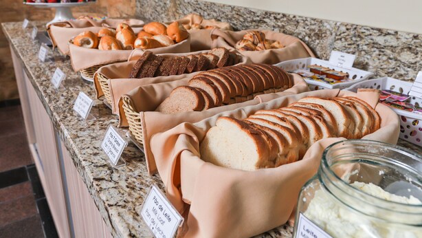 Vitrine de padaria com diversos pães e doces, incluindo um pão de forma e croissants, sobre um balcão de granito.