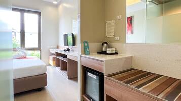 Quarto de hotel moderno com uma cama, um pequeno frigorífico, uma máquina de café e um espelho na parede.