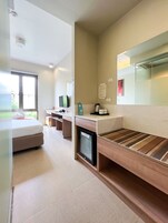 Quarto de hotel moderno com uma cama, um pequeno frigorífico, uma máquina de café e um espelho na parede.