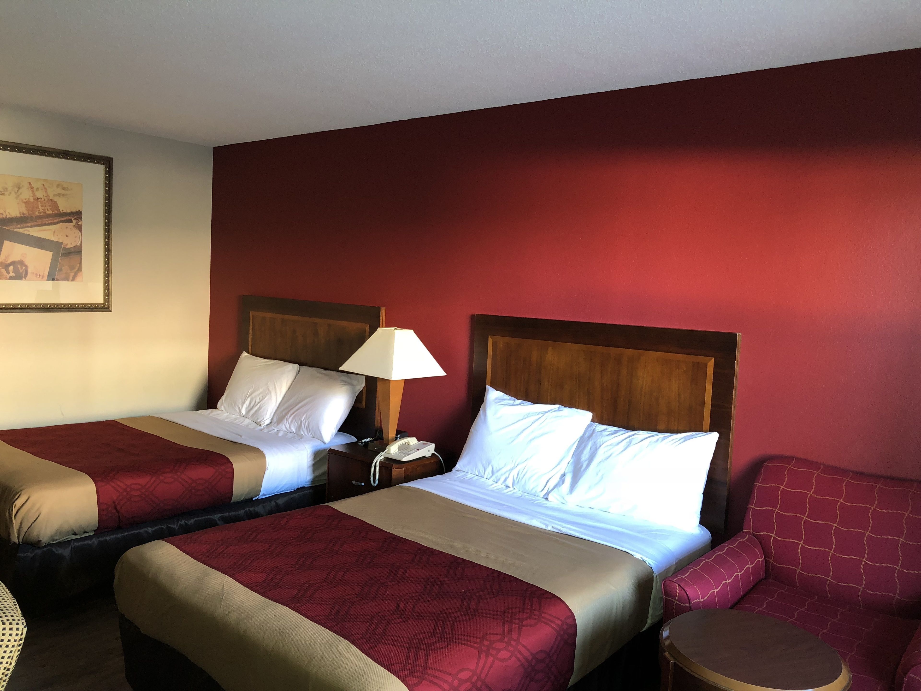Quarto de hotel com duas camas, parede vermelha e cabeceira de madeira.