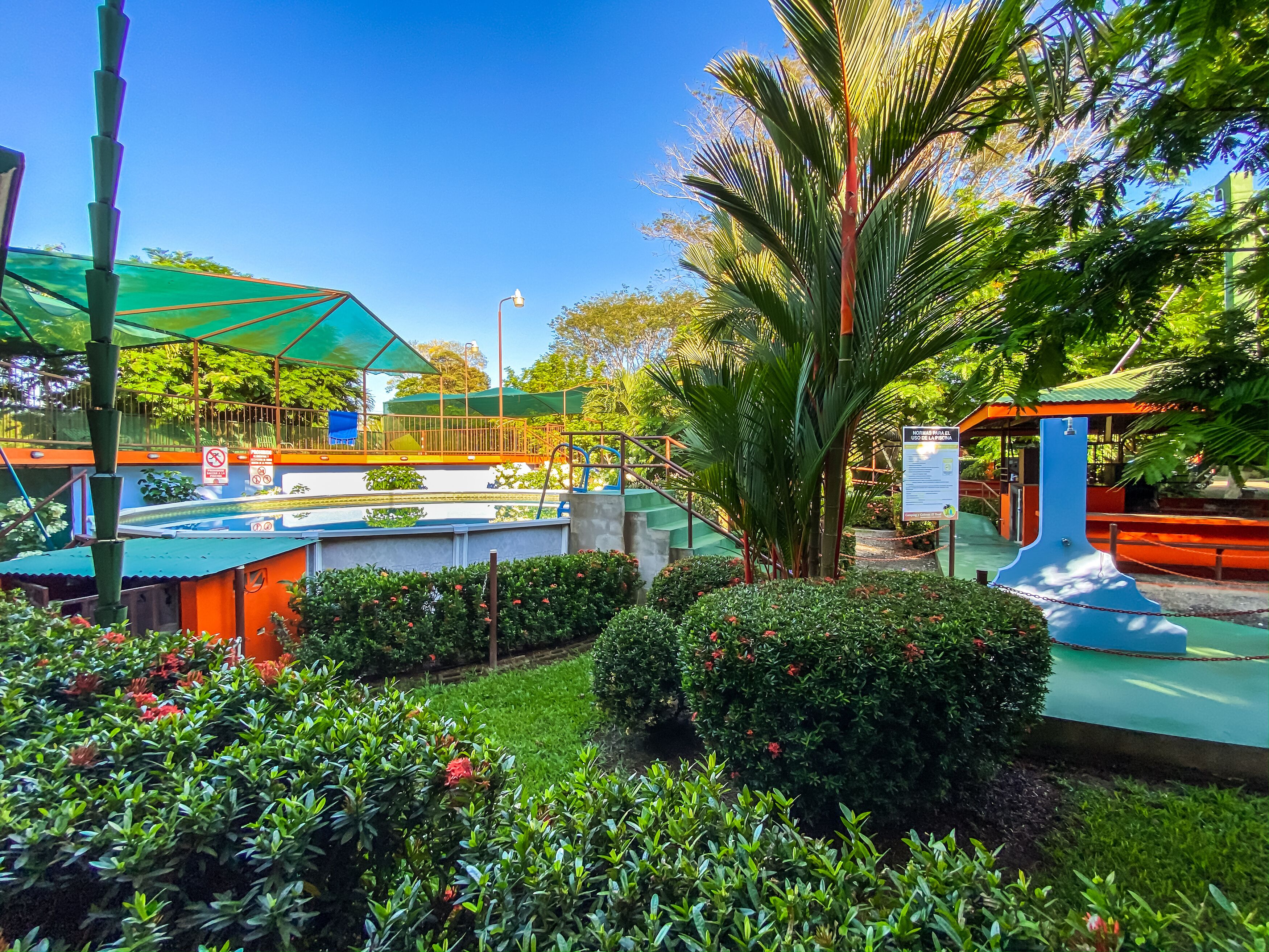 Área externa bem cuidada com piscina, guarda-sóis verdes e placa indicando que não é permitido nadar.