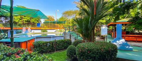 Área externa bem cuidada com piscina, guarda-sóis verdes e placa indicando que não é permitido nadar.
