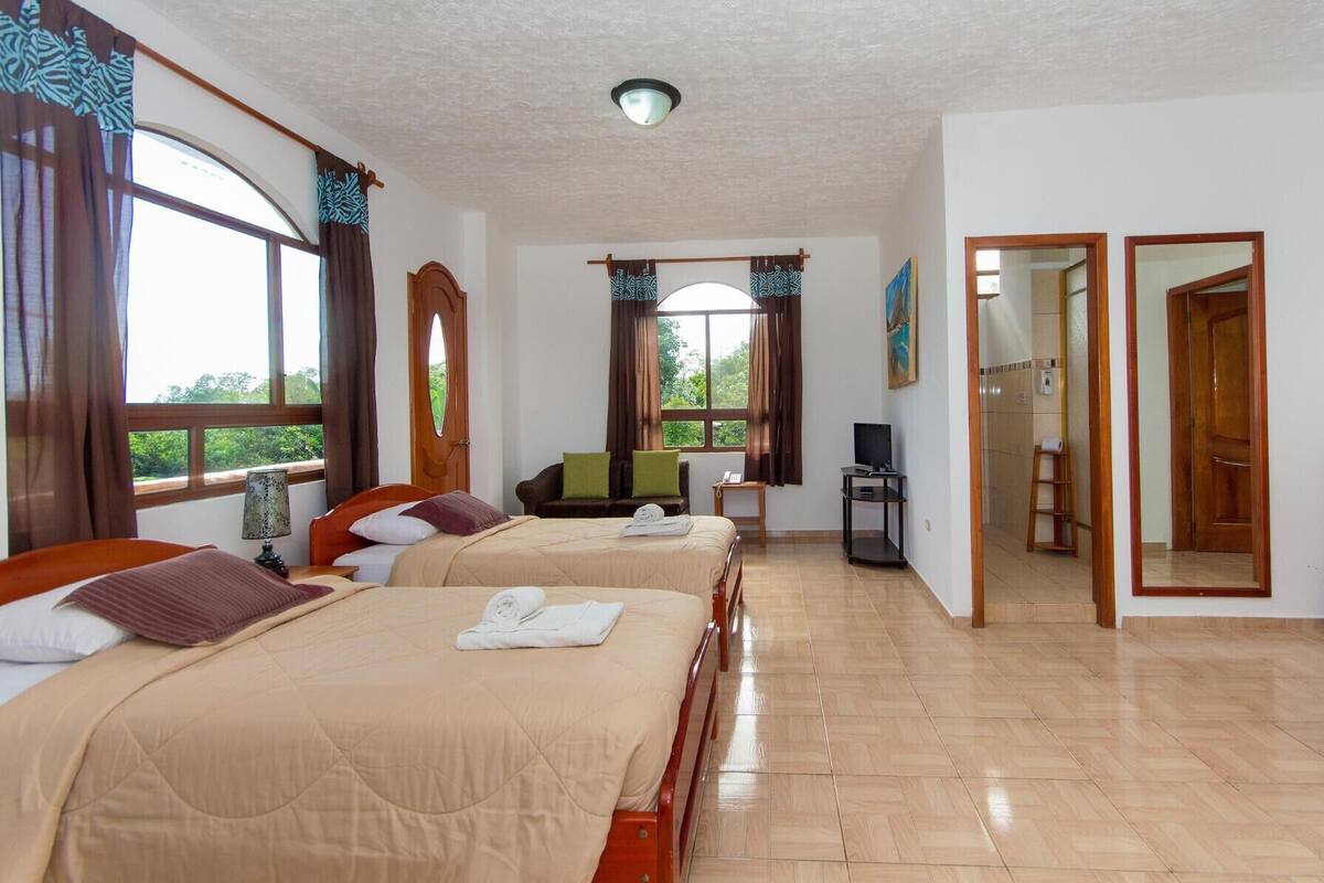 Quarto de hotel com duas camas, televisão, escrivaninha e banheiro visível por uma porta aberta.