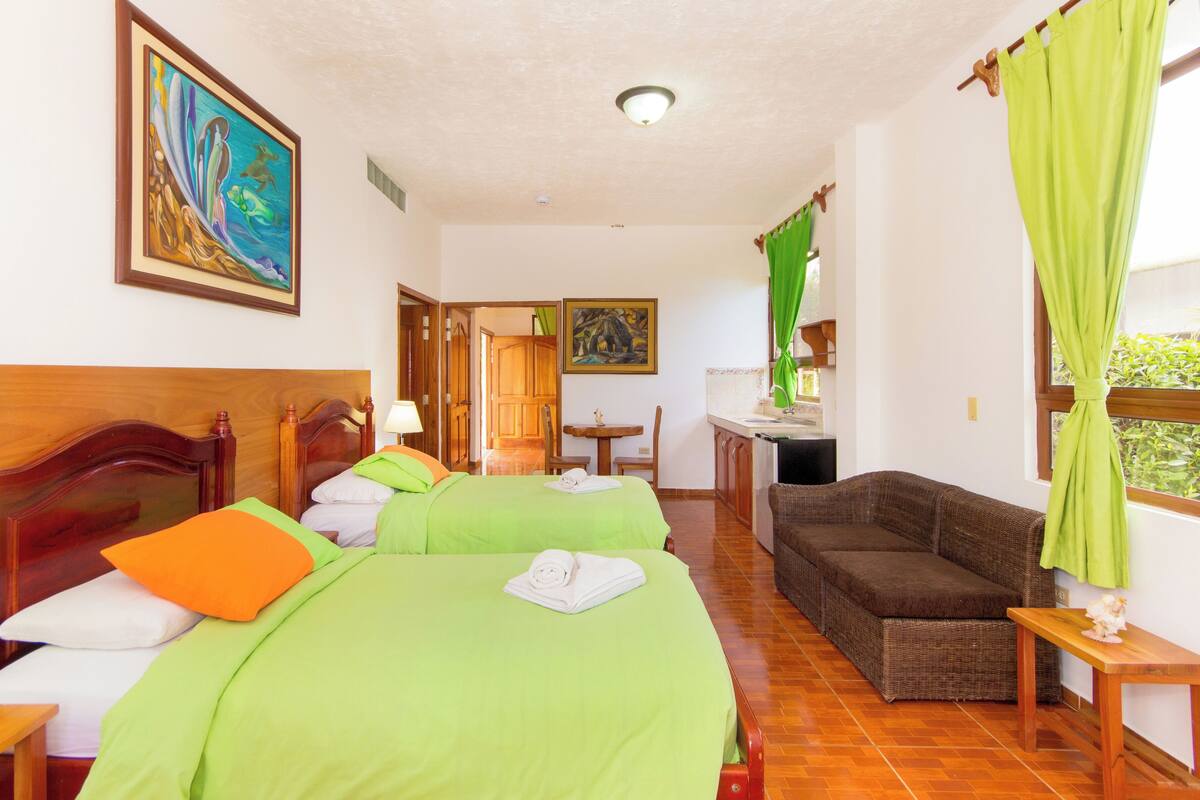 Quarto de hotel com duas camas, um sofá, uma mesa de jantar e um quadro na parede.