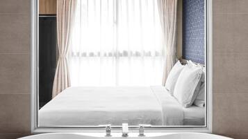 Um banheiro moderno com uma banheira independente, um espelho grande e vista para um quarto com cama e cortinas.