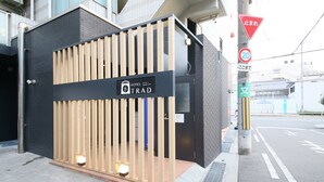 Entrada de um hotel moderno com fachada preta, ripas de madeira e uma placa com o texto 'HOTEL TRAD'.