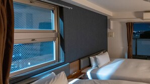 Quarto de hotel com duas camas, uma janela com cortinas, uma cabeceira e um ar condicionado fixado na parede.