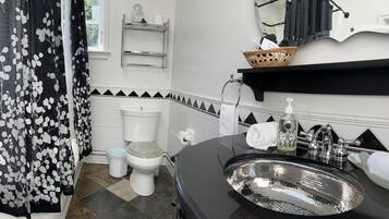 Um banheiro com pia preta, vaso sanitário branco e cortina de chuveiro estampada com flores.