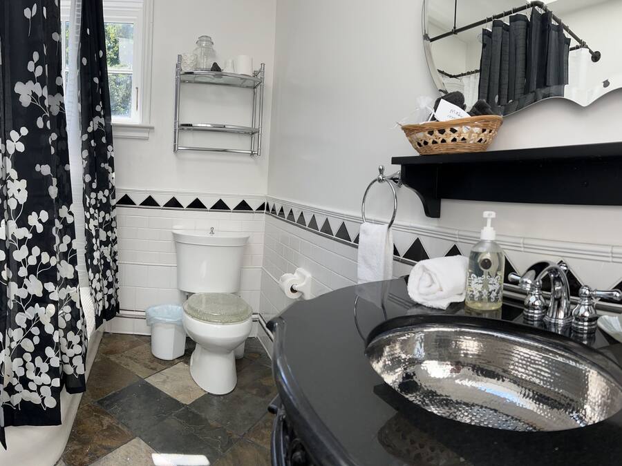Um banheiro com pia preta, vaso sanitário branco e cortina de chuveiro estampada com flores.