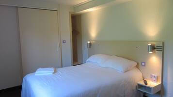 Quarto de hotel com uma cama, mesa de cabeceira com controle remoto e armário com roupas penduradas.