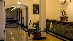 Um saguão de hotel com piso de mármore, uma recepção com parede de pedra decorativa e um lustre.