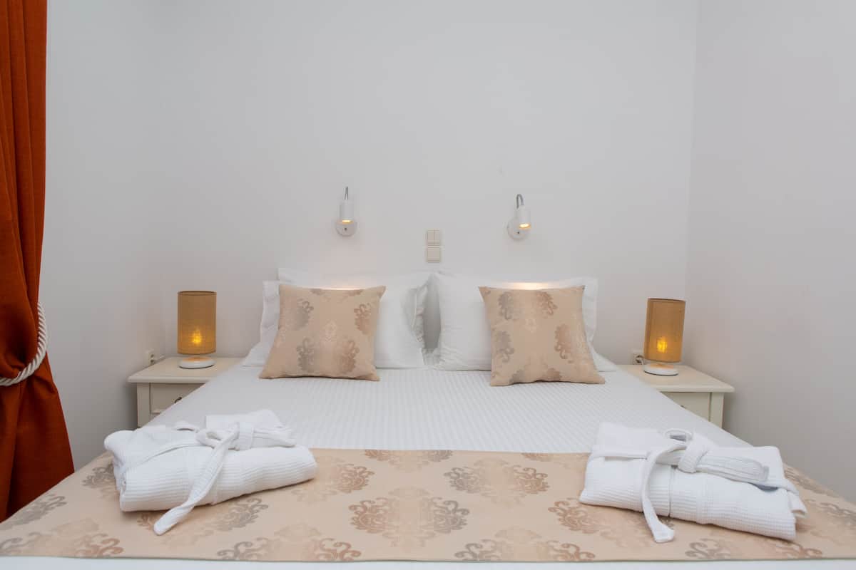 Quarto de hotel com cama, duas luminárias laterais, mesa de cabeceira e um roupão sobre a cama.
